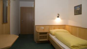 Quarto pequeno com cama de solteiro, cabeceira de madeira, mesa de cabeceira e luz acoplada na parede.