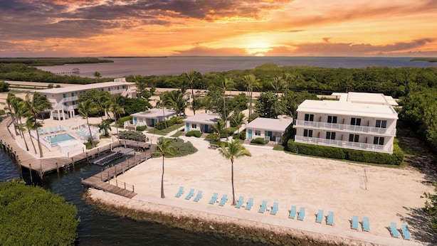 Um hotel à beira-mar com piscina, espreguiçadeiras e vista para o oceano ao pôr do sol.