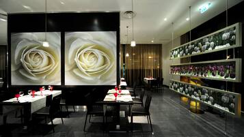 Um restaurante moderno com design minimalista, destacando uma grande obra de arte floral na parede e uma exposição de tulipas. As mesas estão dispostas com copos de vinho tinto e toalhas de mesa brancas.