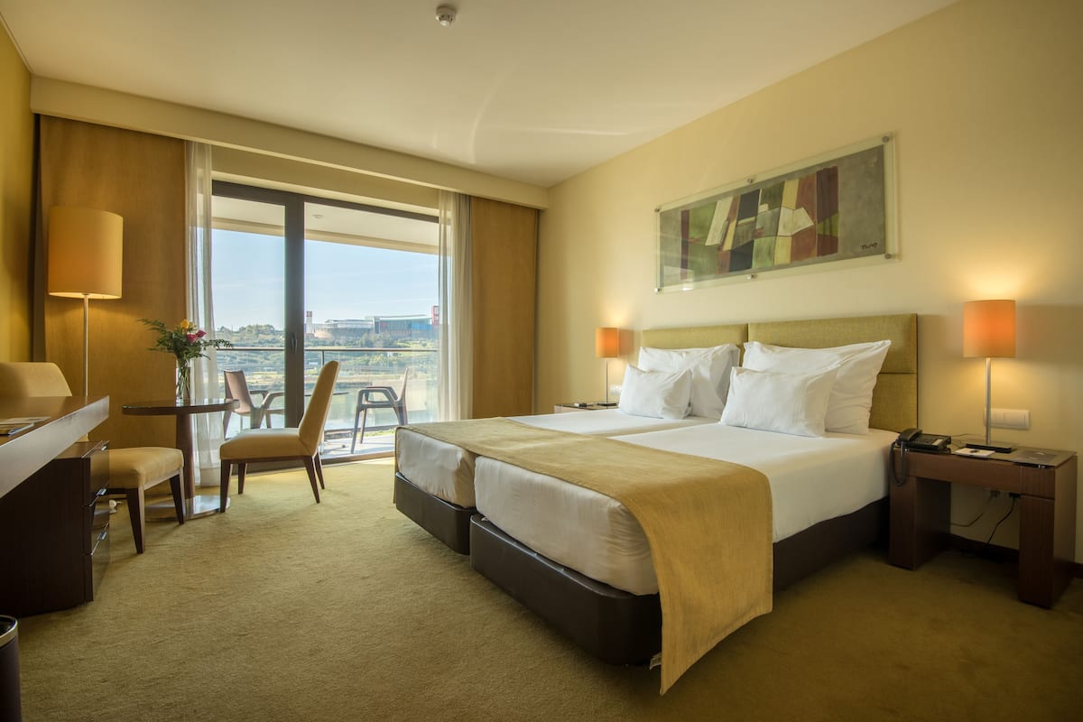 Quarto de hotel com cama grande, escrivaninha, cadeira e vista da cidade.