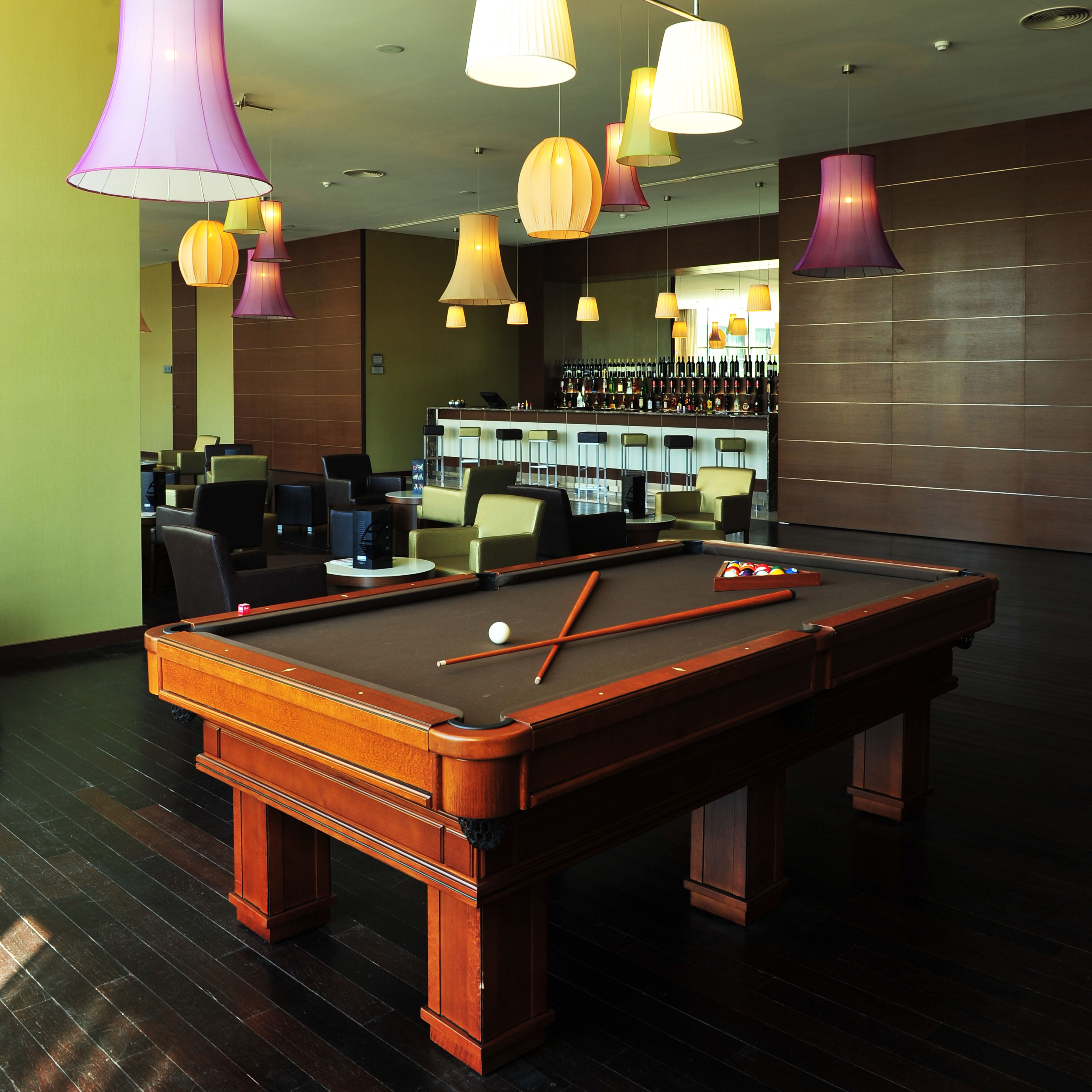 Uma mesa de bilhar com bolas, um espaço de bar com garrafas e várias luminárias pendentes.