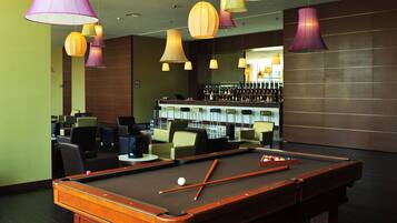 Uma mesa de bilhar com bolas, um espaço de bar com garrafas e várias luminárias pendentes.