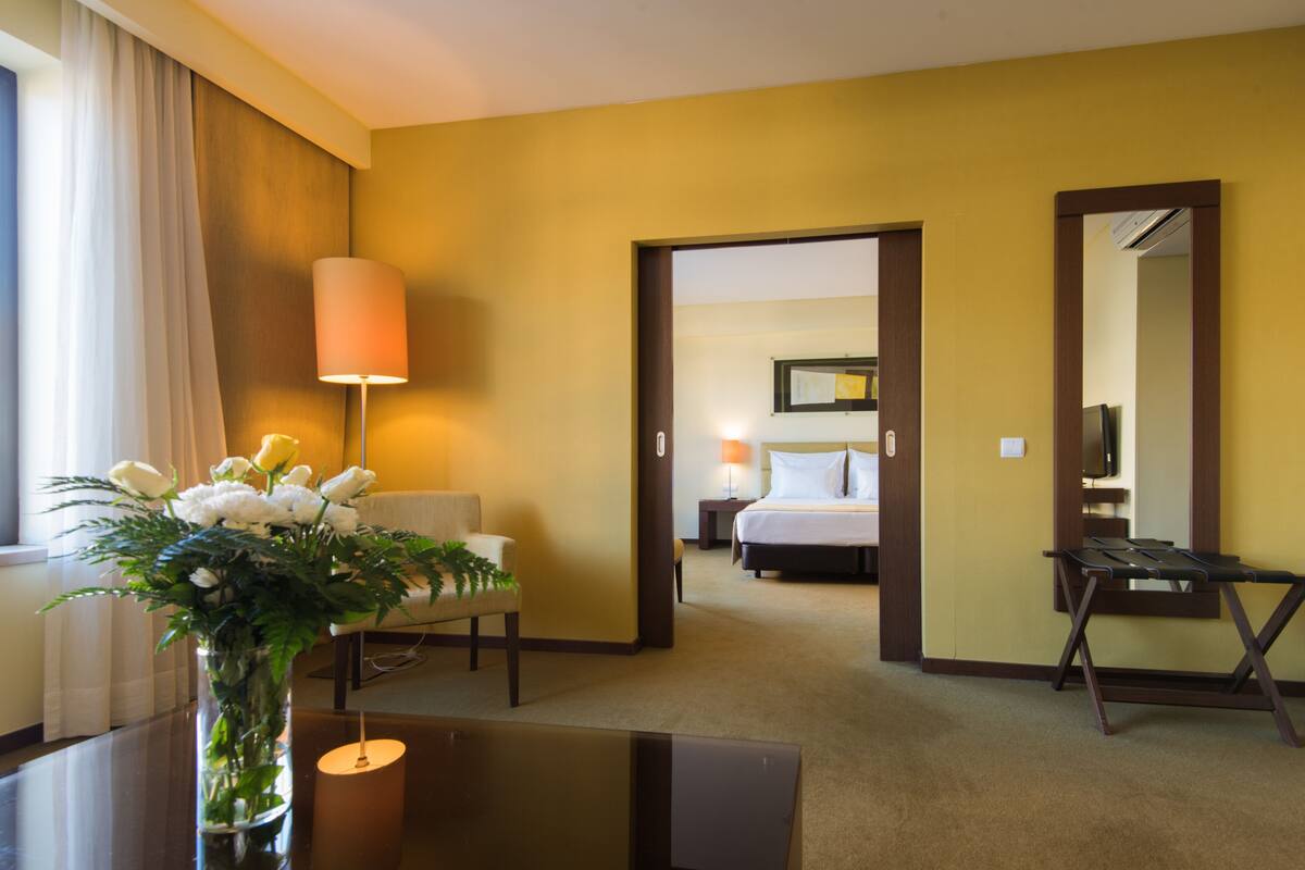 Quarto de hotel com cama, mesa de cabeceira, luminária, cadeira e espelho.