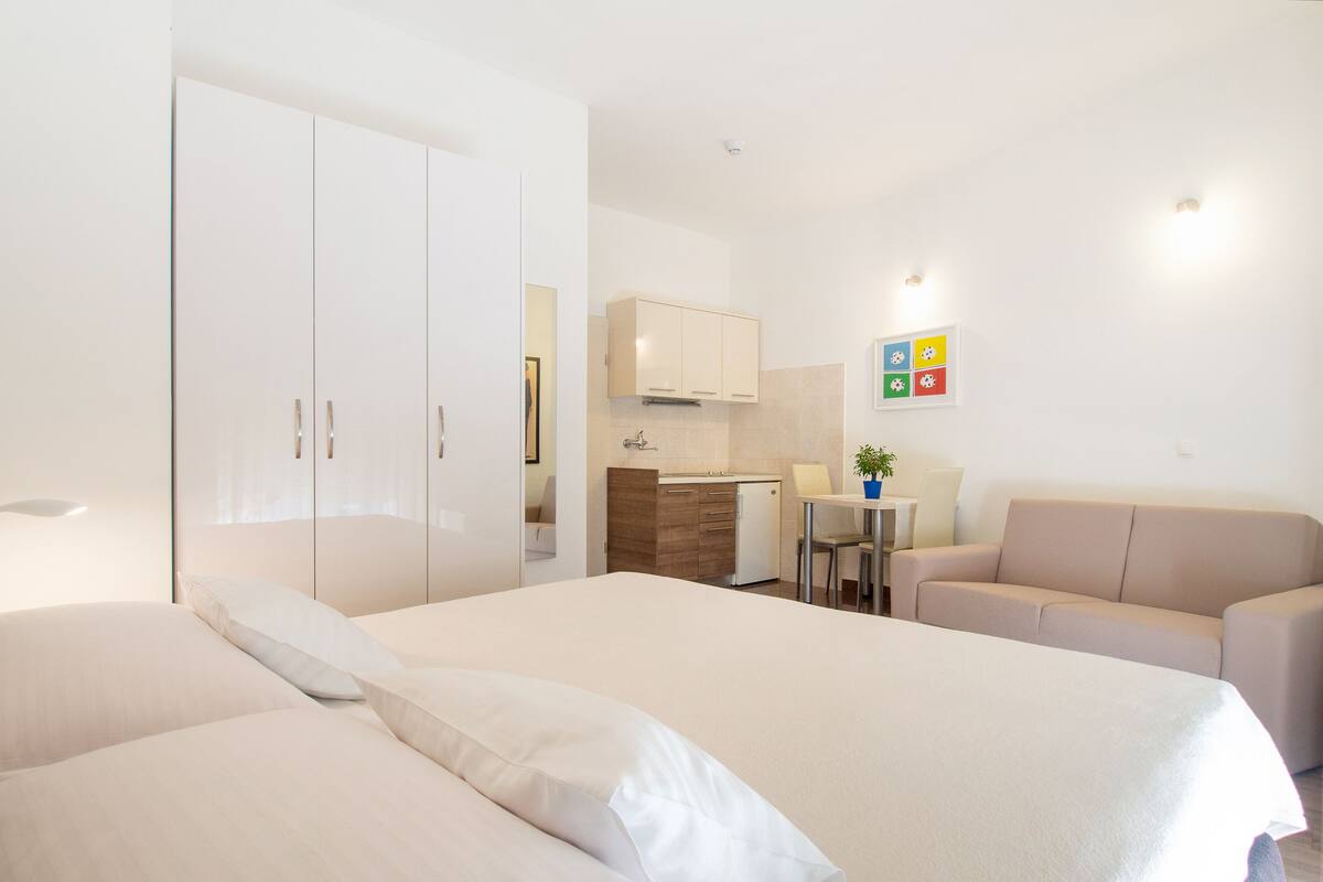 Quarto de hotel moderno com uma cama grande, um sofá, uma pequena cozinha e uma mesa de jantar.