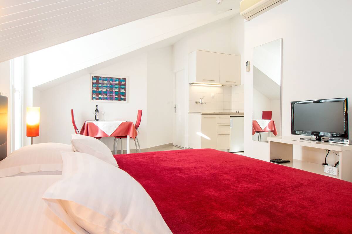 Quarto de hotel com cama, escrivaninha, cadeira, televisão e banheiro.