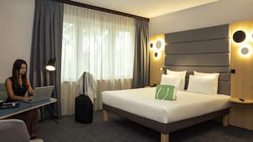 Quarto de hotel com cama, escrivaninha, um laptop, mala e cadeira.