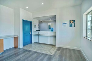 Um corredor com uma porta azul, uma mesa de recepção e uma janela à direita.