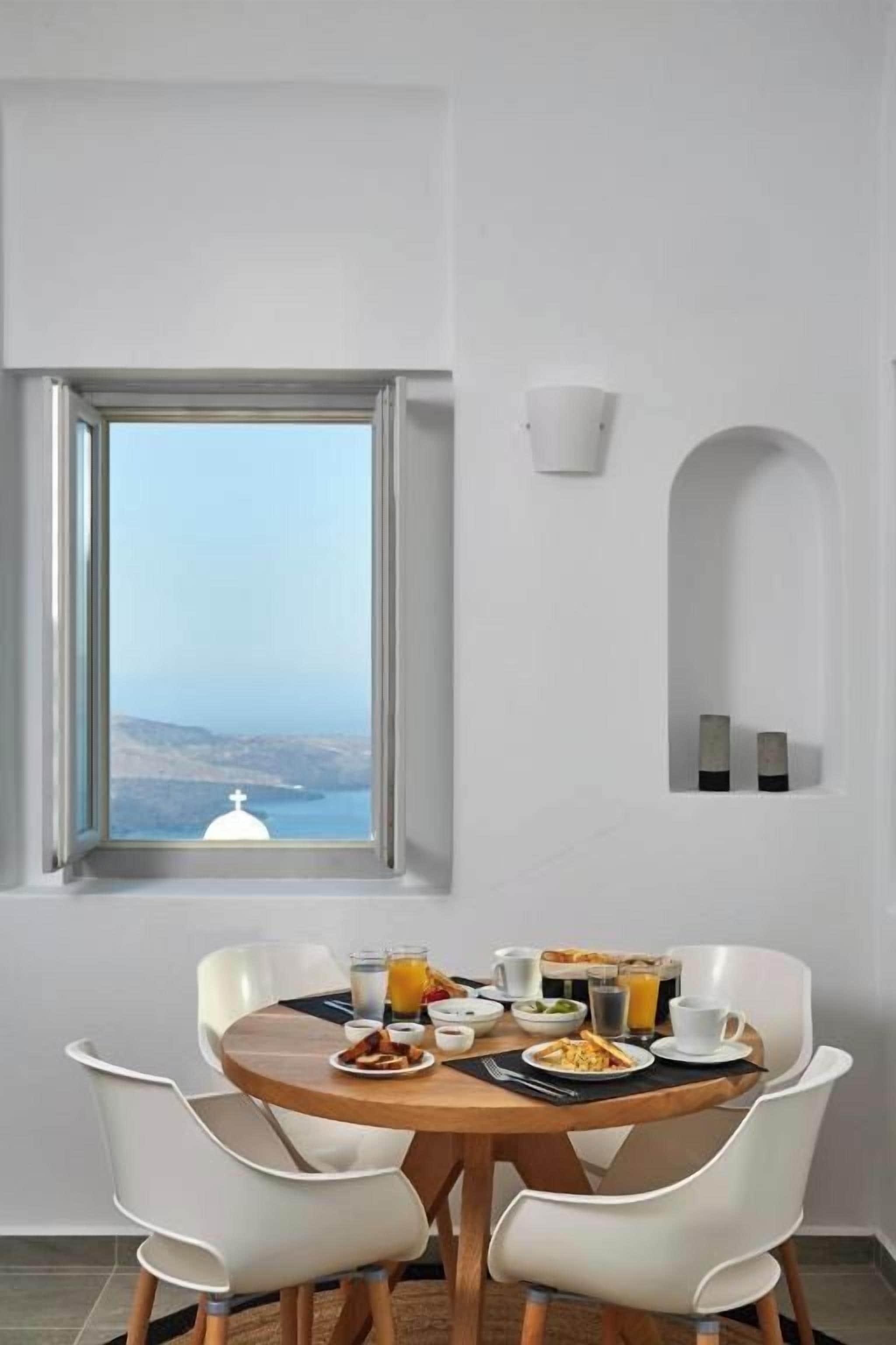 Uma sala de jantar com mesa posta para café da manhã, janela com vista e parede branca com luminária.