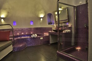 Um quarto de spa com chuveiro em cabine de vidro, uma banheira separada e um espaço de estar com um almofada vermelha.