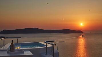 Vista do pôr do sol a partir de uma varanda com piscina, dois copos de vinho e uma garrafa.