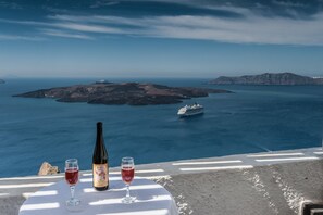 Uma mesa com uma garrafa e copos de vinho, com vista para um mar calmo e uma ilha distante.