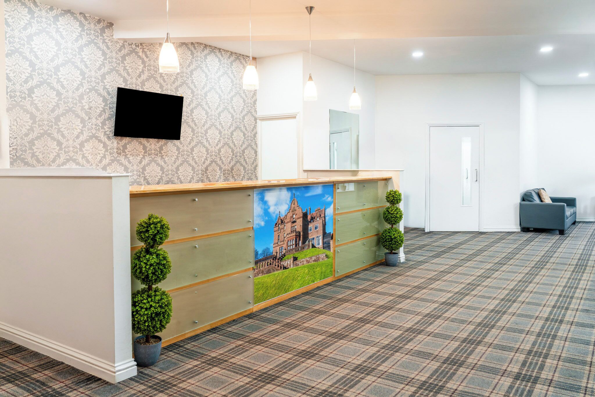 Uma área de recepção com balcão de check-in, uma TV de tela plana na parede e um tapete estampado.