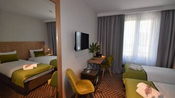 Quarto de hotel com duas camas, uma escrivaninha com cadeira, televisão e uma janela grande com cortinas.