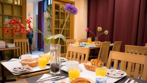 Mesa de café da manhã posta para dois, com croissants, suco de laranja e um vaso de flores.