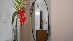 Um quarto com um armário de madeira, um vaso transparente com uma planta e um espelho oval fixado na parede com moldura decorativa.