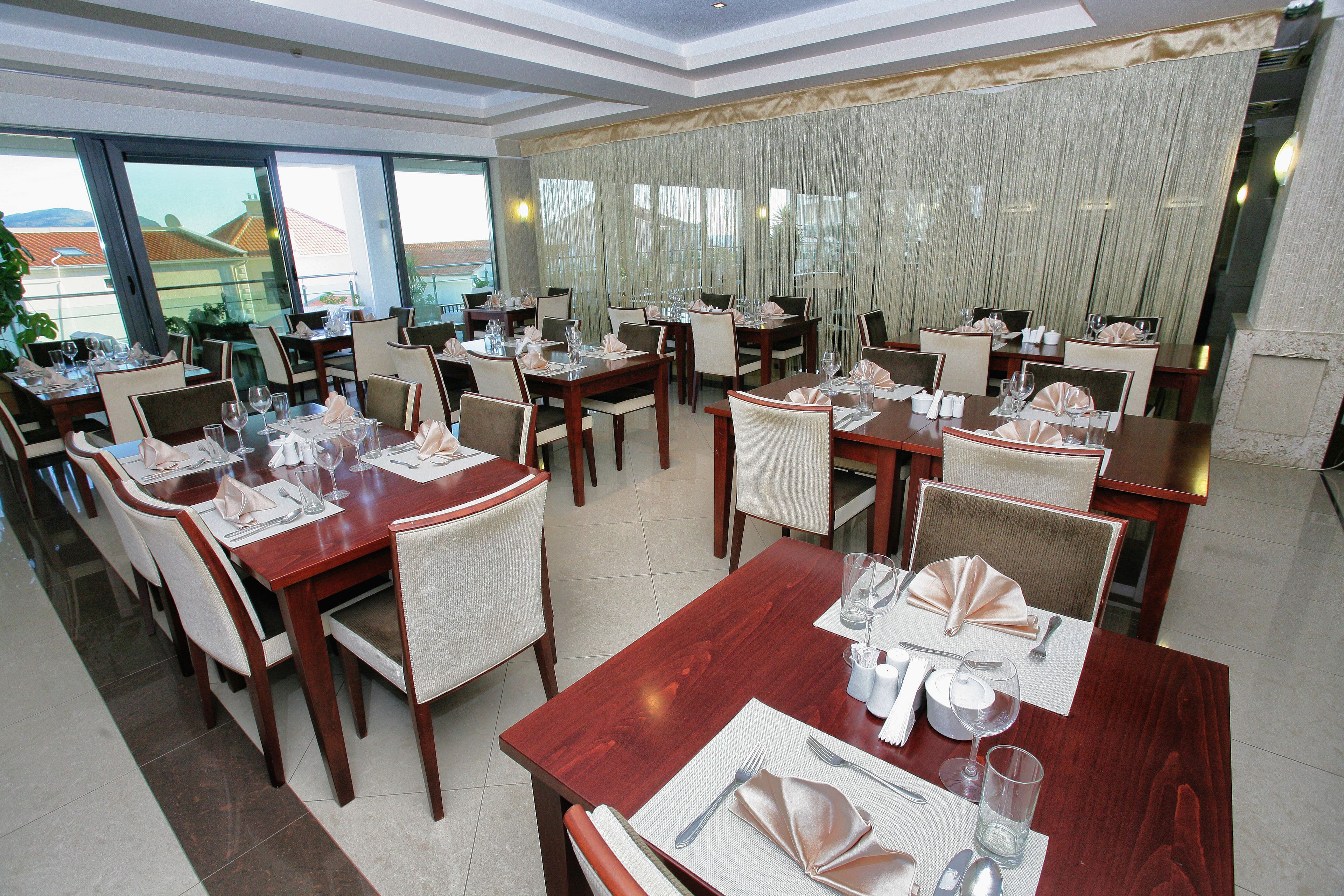Uma sala de jantar com várias mesas preparadas para o serviço, grandes janelas e vista para o exterior.