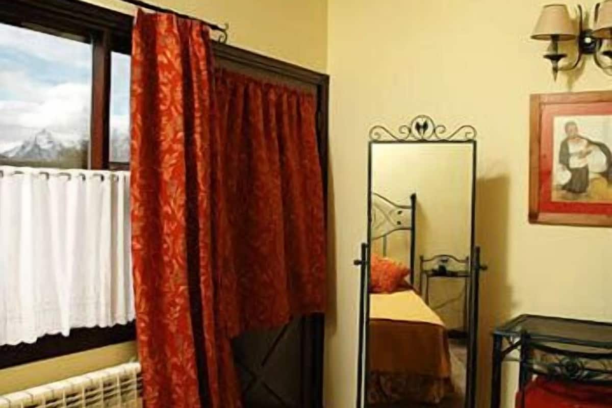 Quarto com cama, janela com cortinas vermelhas, radiador, espelho e pintura na parede.