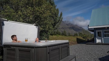 Uma banheira de hidromassagem com duas pessoas, um deck de madeira e montanhas ao fundo.