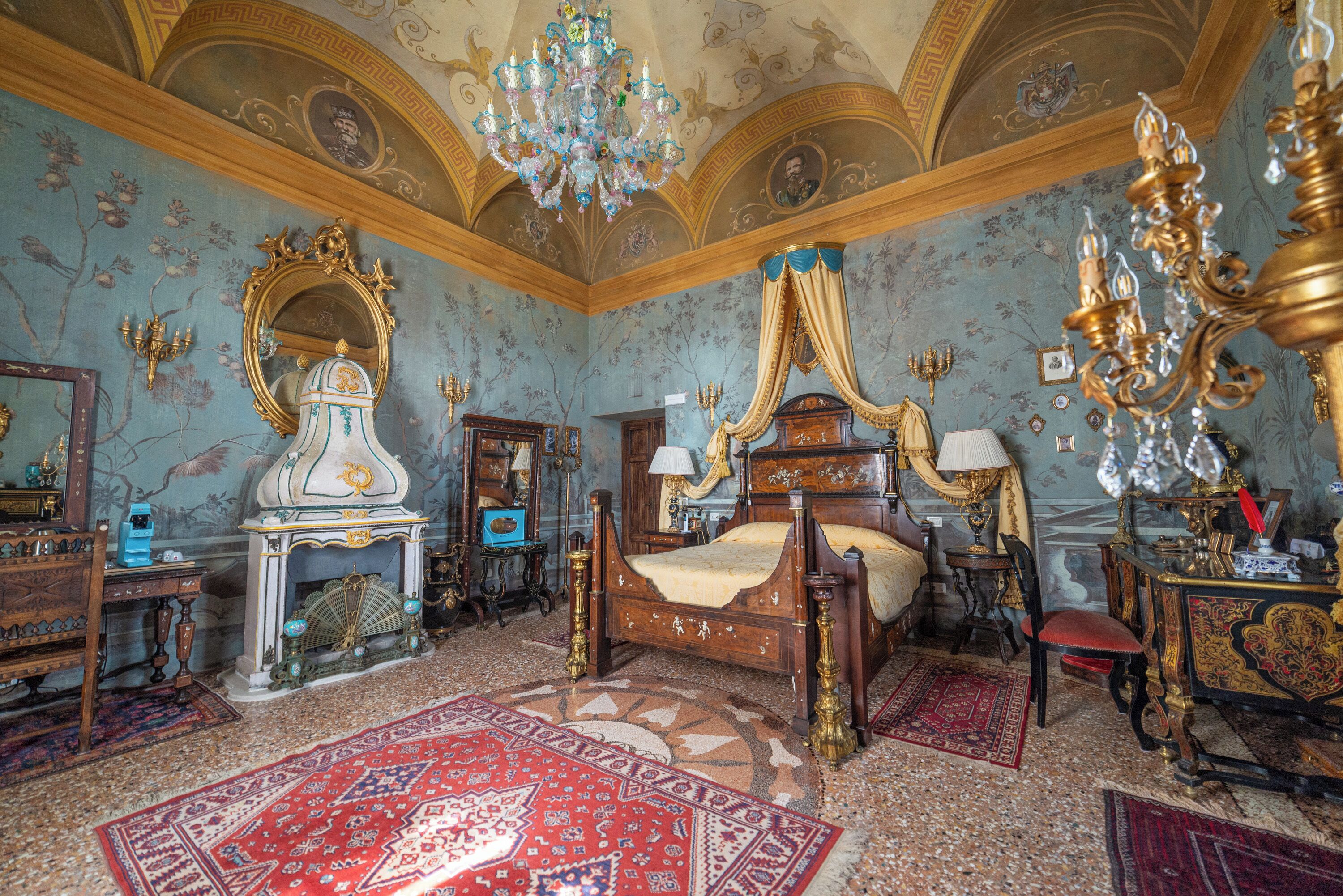Quarto com cama de dossel, lustres ornamentados e um espelho grande.