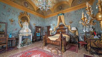 Quarto com cama de dossel, lustres ornamentados e um espelho grande.