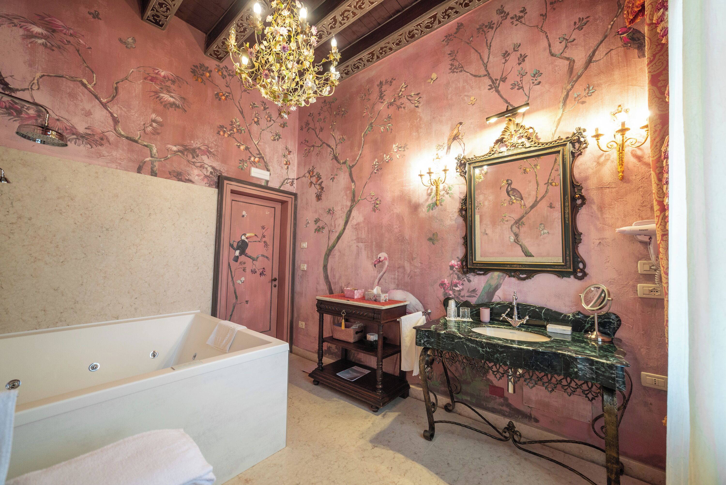 Casa de banho com banheira, toucador, candeeiro de cristal e painel floral.