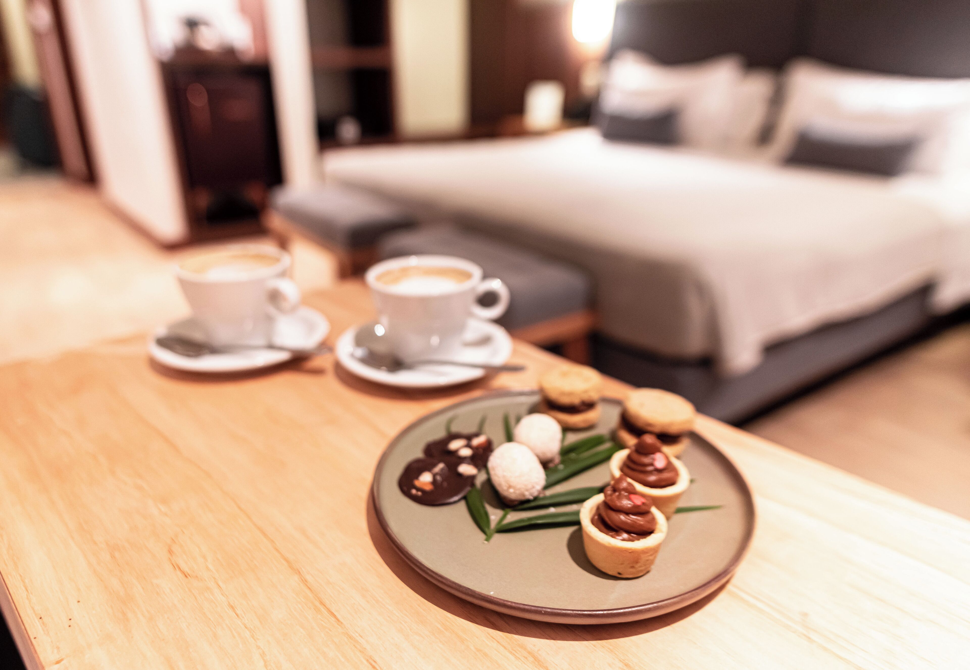 Bandeja de café da manhã com doces e uma xícara de café sobre uma mesa de madeira em quarto de hotel.