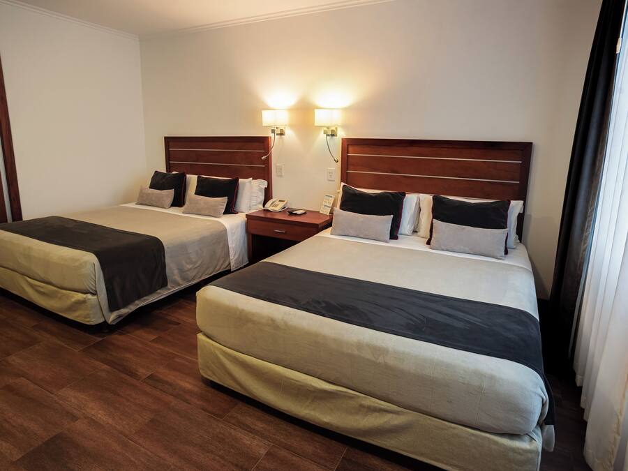 Quarto de hotel com duas camas, cabeceiras de madeira, mesas de cabeceira com luminárias e um telefone.
