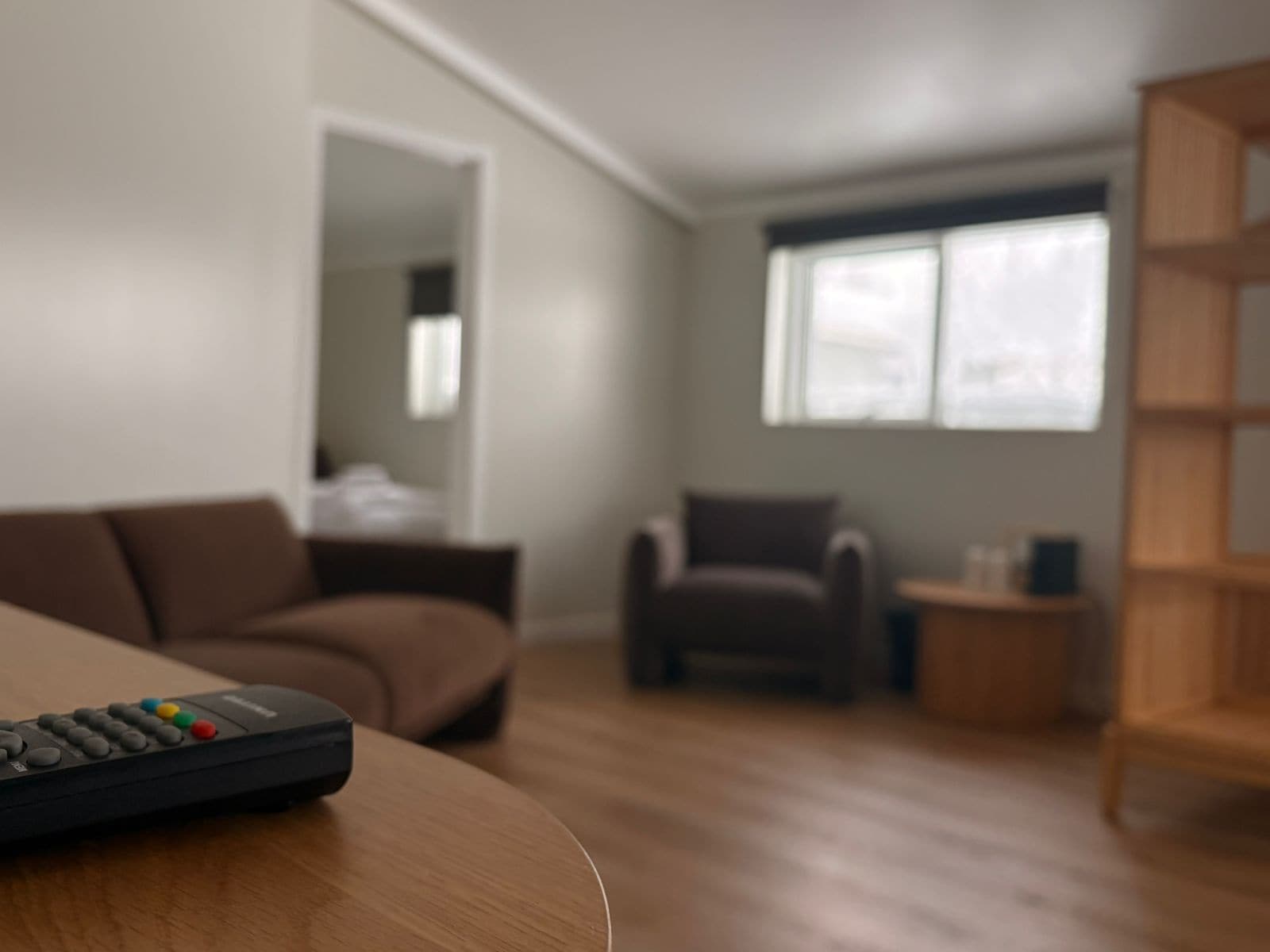 Um controle remoto sobre uma mesa de madeira em uma sala de estar com um sofá marrom, uma cadeira e uma estante.