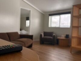 Um controle remoto sobre uma mesa de madeira em uma sala de estar com um sofá marrom, uma cadeira e uma estante.