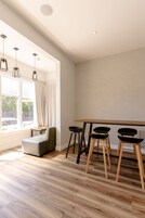 Uma cozinha moderna com mesa de madeira e banquetas pretas, um sofá cinza e luminárias pendentes.