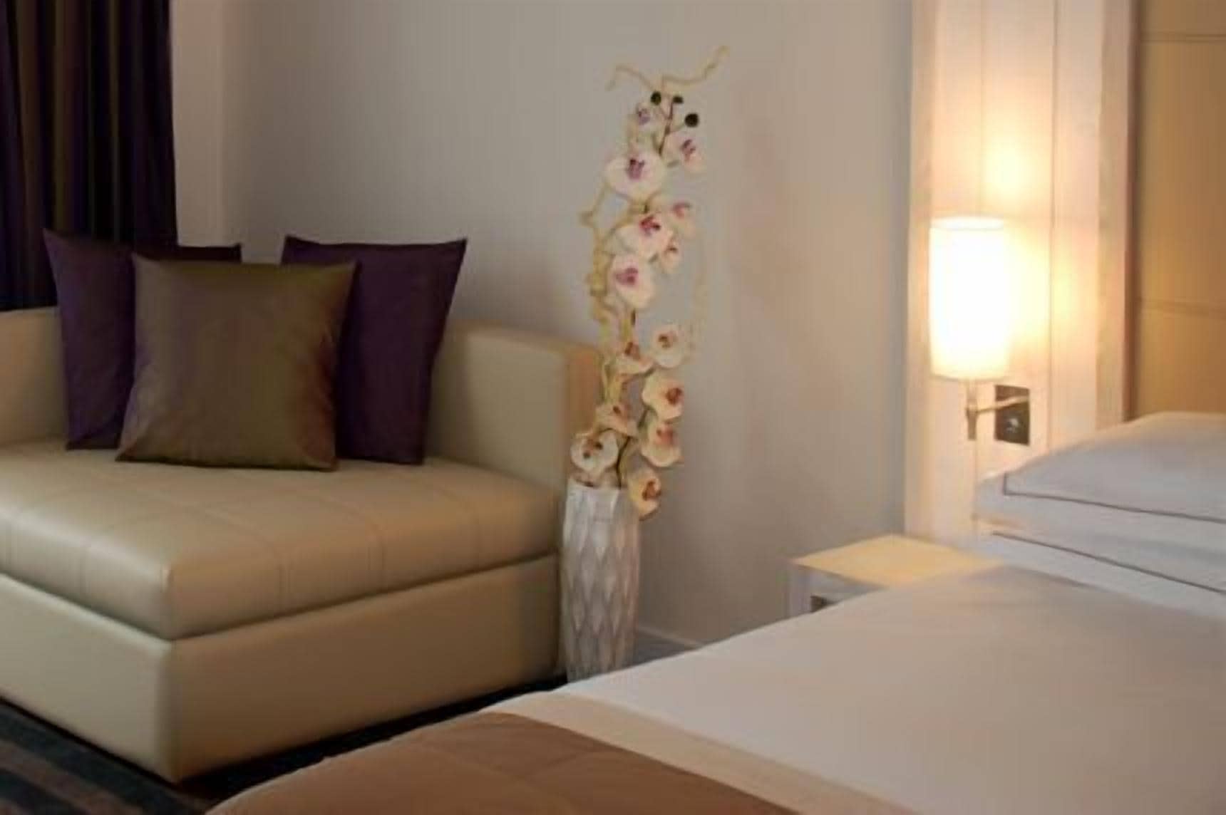 Quarto de hotel com cama, sofá e uma planta decorativa.