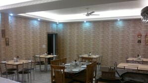 Uma sala de jantar com várias mesas e cadeiras, um ventilador de teto e uma parede revestida com azulejos.