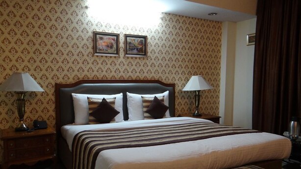 Quarto de hotel com uma cama grande, duas luminárias de cabeceira, uma mesa de cabeceira, uma pequena mesa e um travesseiro decorativo.