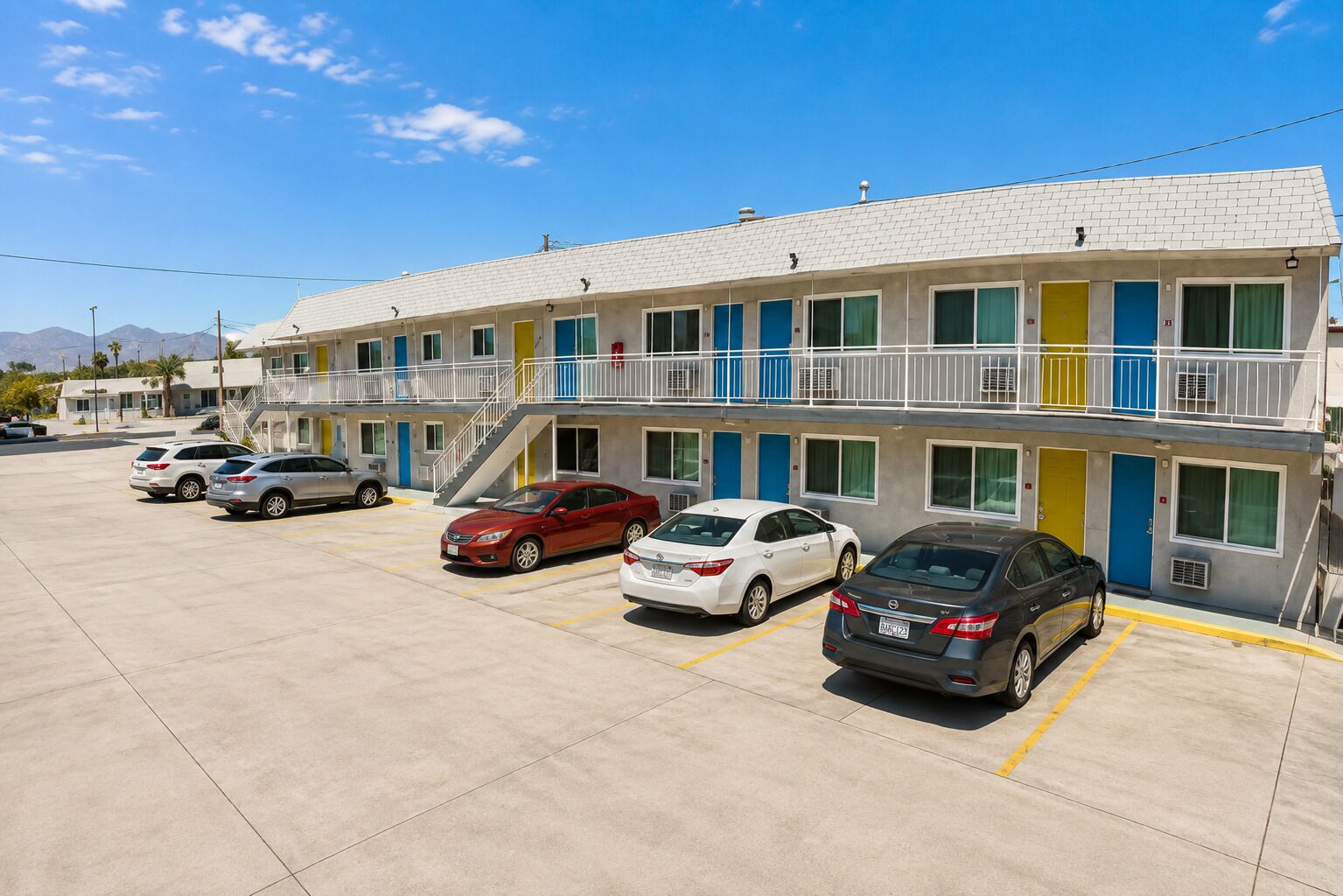 Um motel com estacionamento, vários carros estacionados e céu claro.