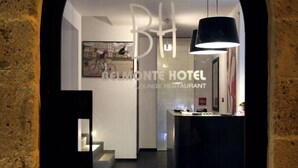 Um saguão de hotel com design moderno, apresentando uma mesa de recepção, uma luminária pendente grande e um quadro na parede.