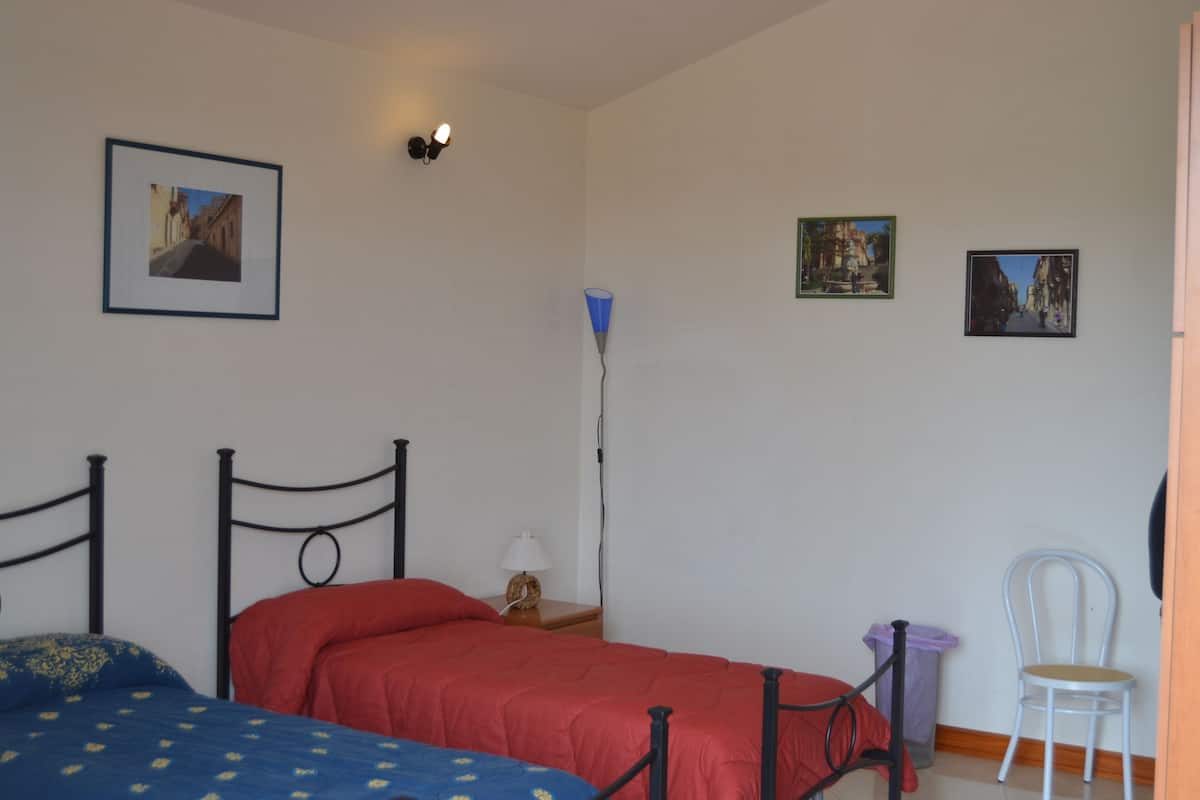 Quarto com duas camas, uma mesa de cabeceira, uma luminária e uma cadeira.