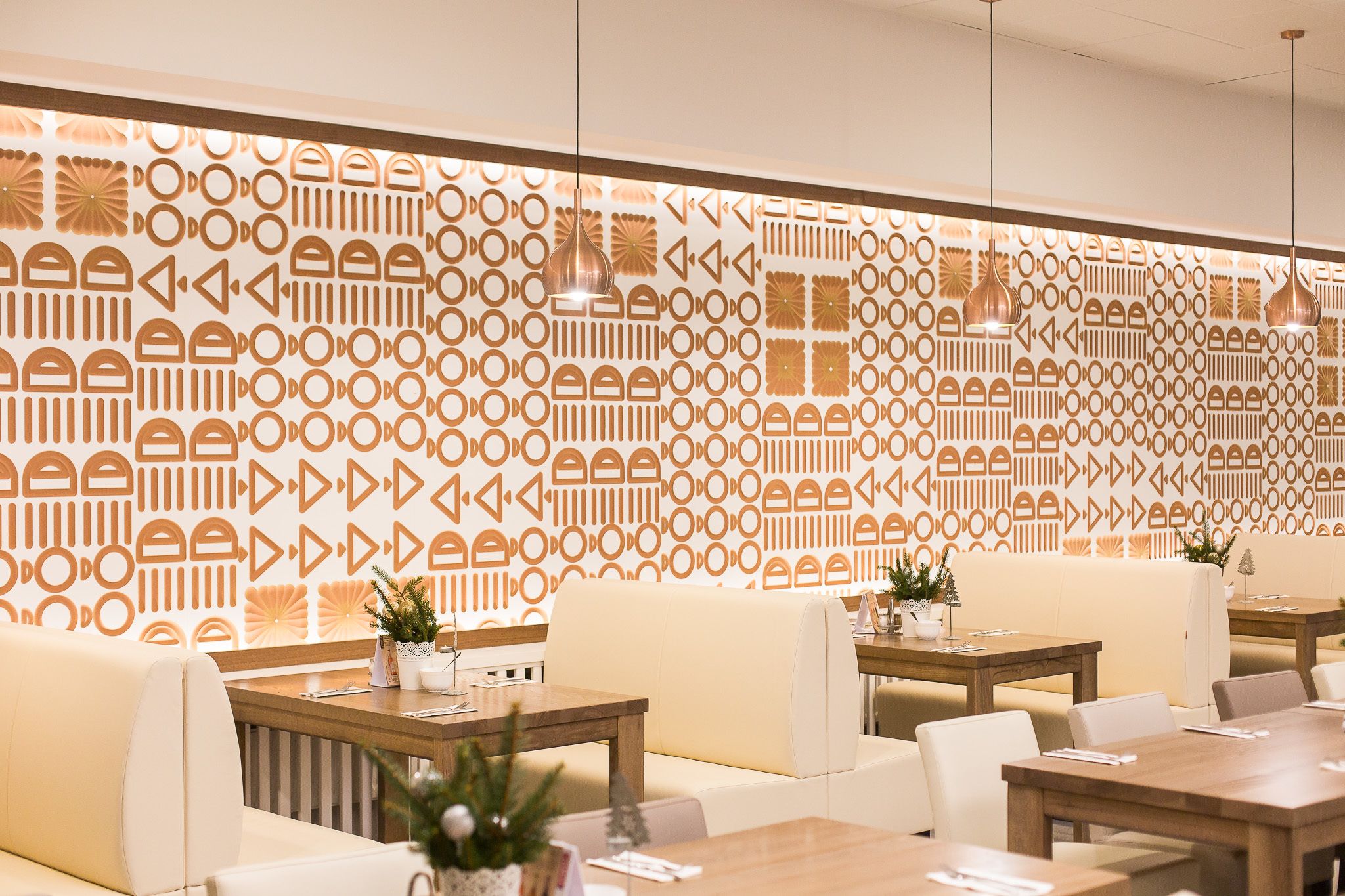 Interior de restaurante moderno com decoração de parede estampada, mesas de madeira e assentos acolchoados brancos.