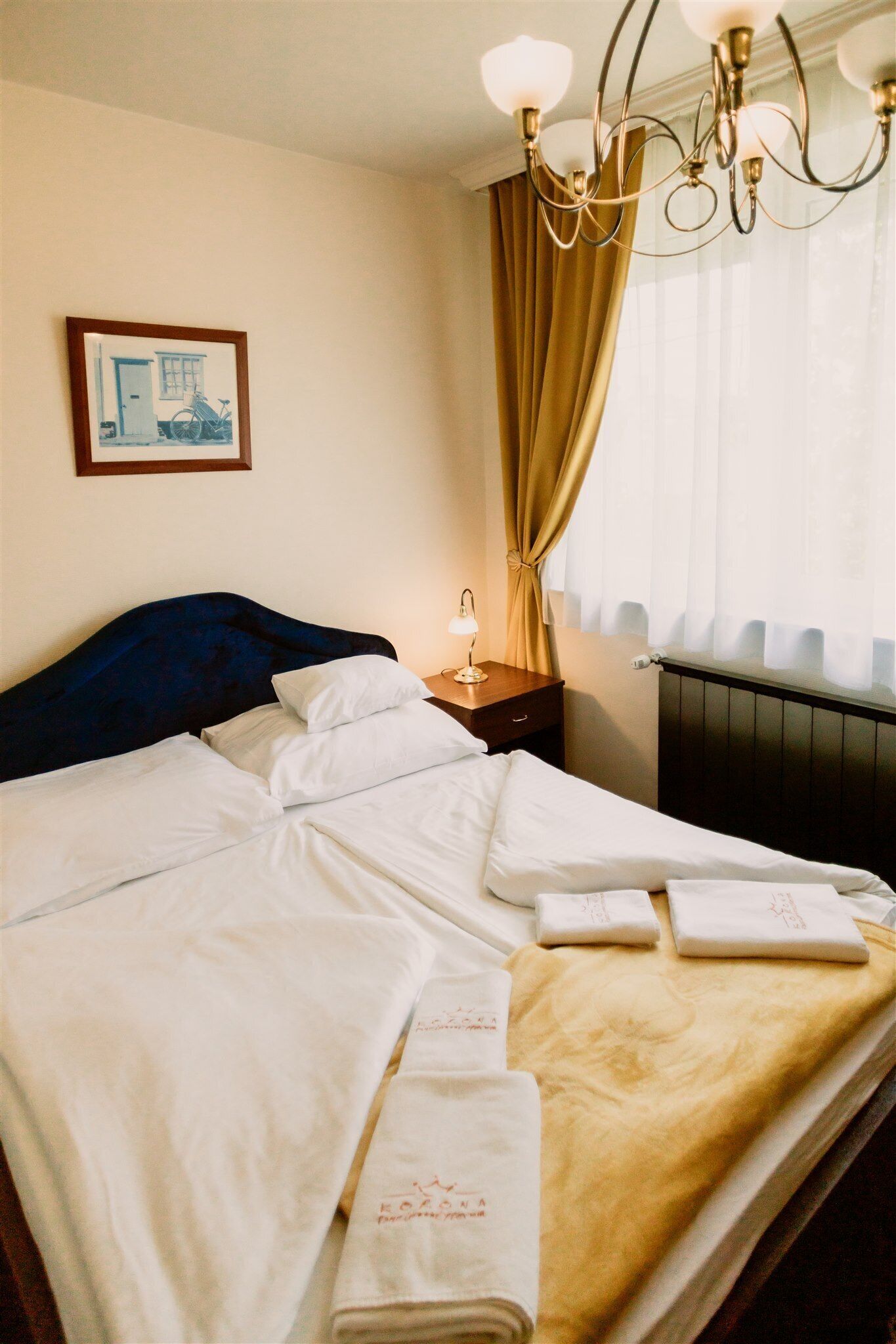 Cama bem arrumada com lençóis brancos, abajur e quadro na parede.