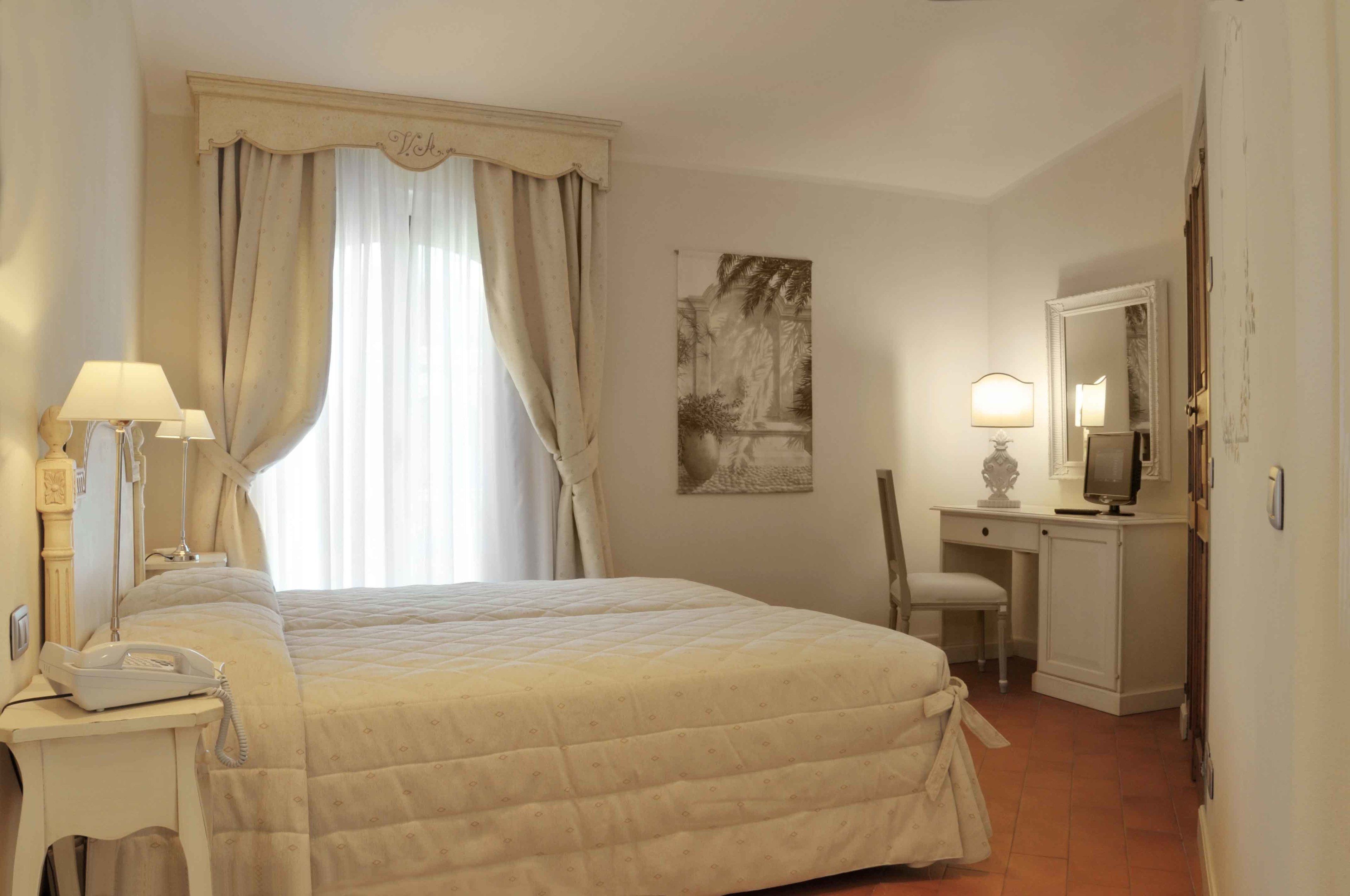 Quarto de hotel com cama, escrivaninha com cadeira, telefone e um quadro na parede.
