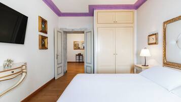 Quarto de hotel com uma cama, televisão, escrivaninha com candeeiro e guarda-roupa.