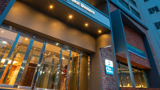 Entrada de hotel moderna com portas de vidro, uma placa em destaque com a inscrição 