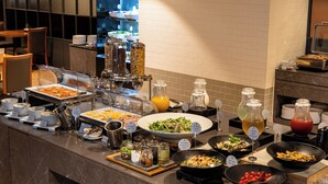 Buffet com diversos alimentos, acompanhamentos e um dispensador de sucos.