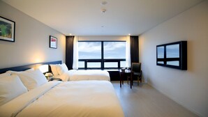 Quarto de hotel com duas camas, uma escrivaninha e uma janela grande com vista.