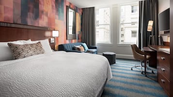 Quarto de hotel com uma cama grande, uma mesa, uma cadeira e vista da cidade pela janela.