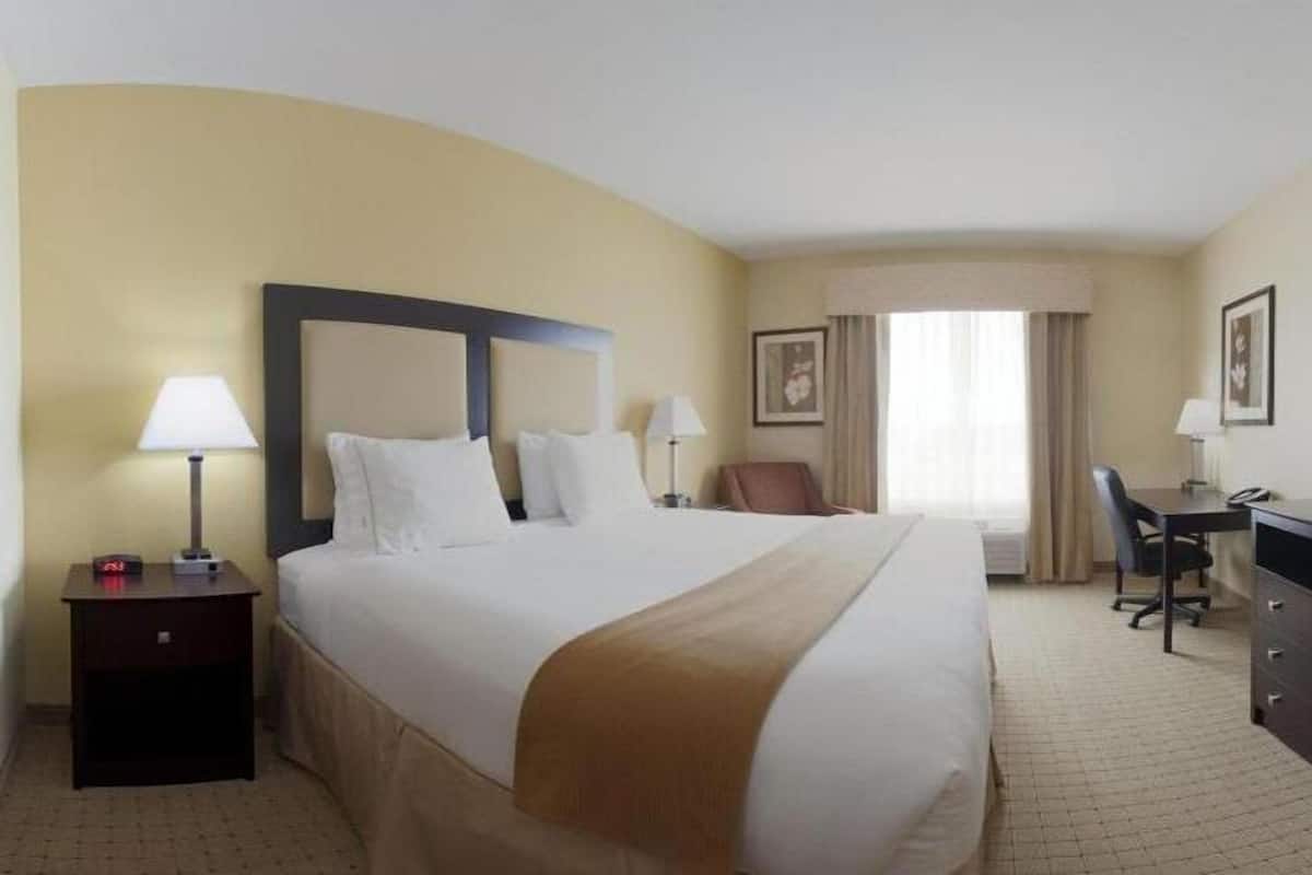 Quarto de hotel com uma cama grande, uma escrivaninha, uma cadeira e um pequeno sofá.