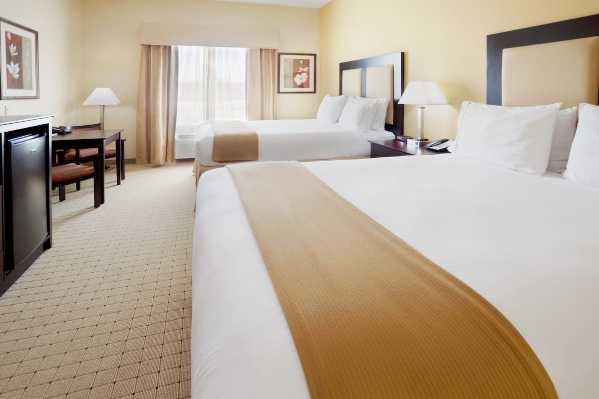 Quarto de hotel com duas camas, uma escrivaninha e uma cadeira.
