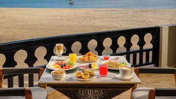 Mesa posta com itens de café da manhã, incluindo waffles, ovos e frutas, com vista para uma praia.