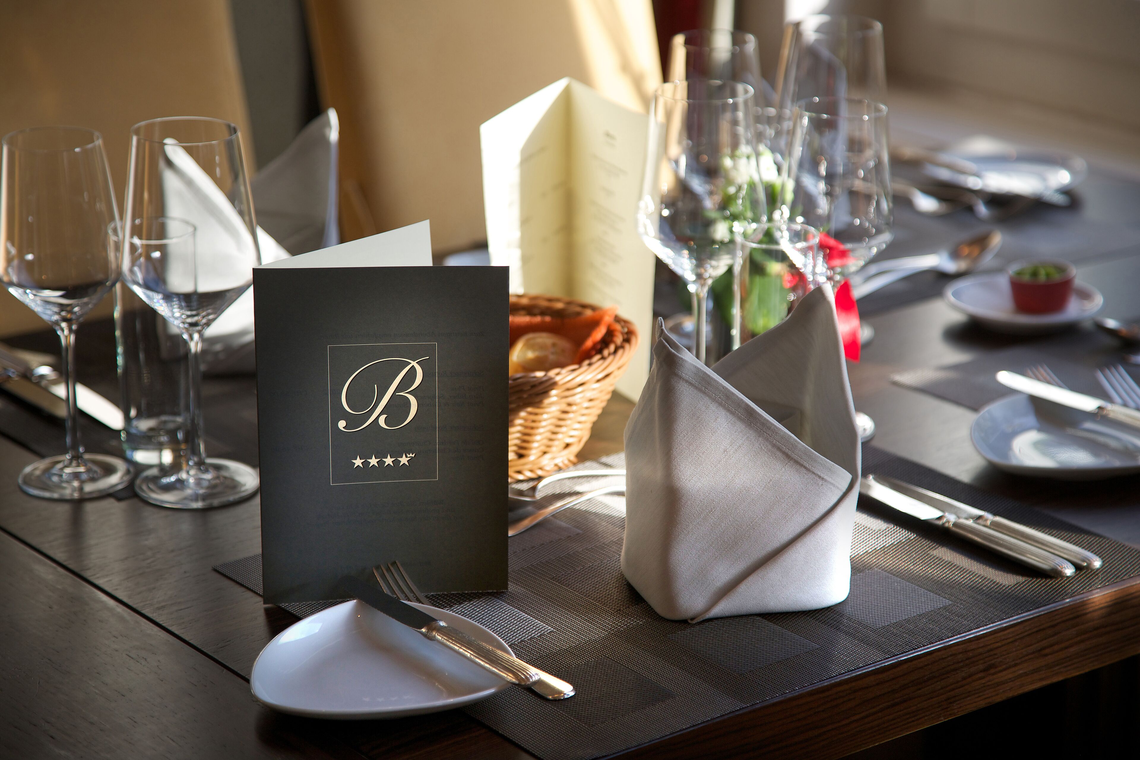 Mesa posta para refeição, com menu, copos de vinho e talheres.