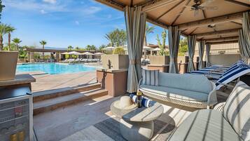 Uma área junto à piscina com espreguiçadeiras, um sofá e uma mesa com uma garrafa e um chapéu.