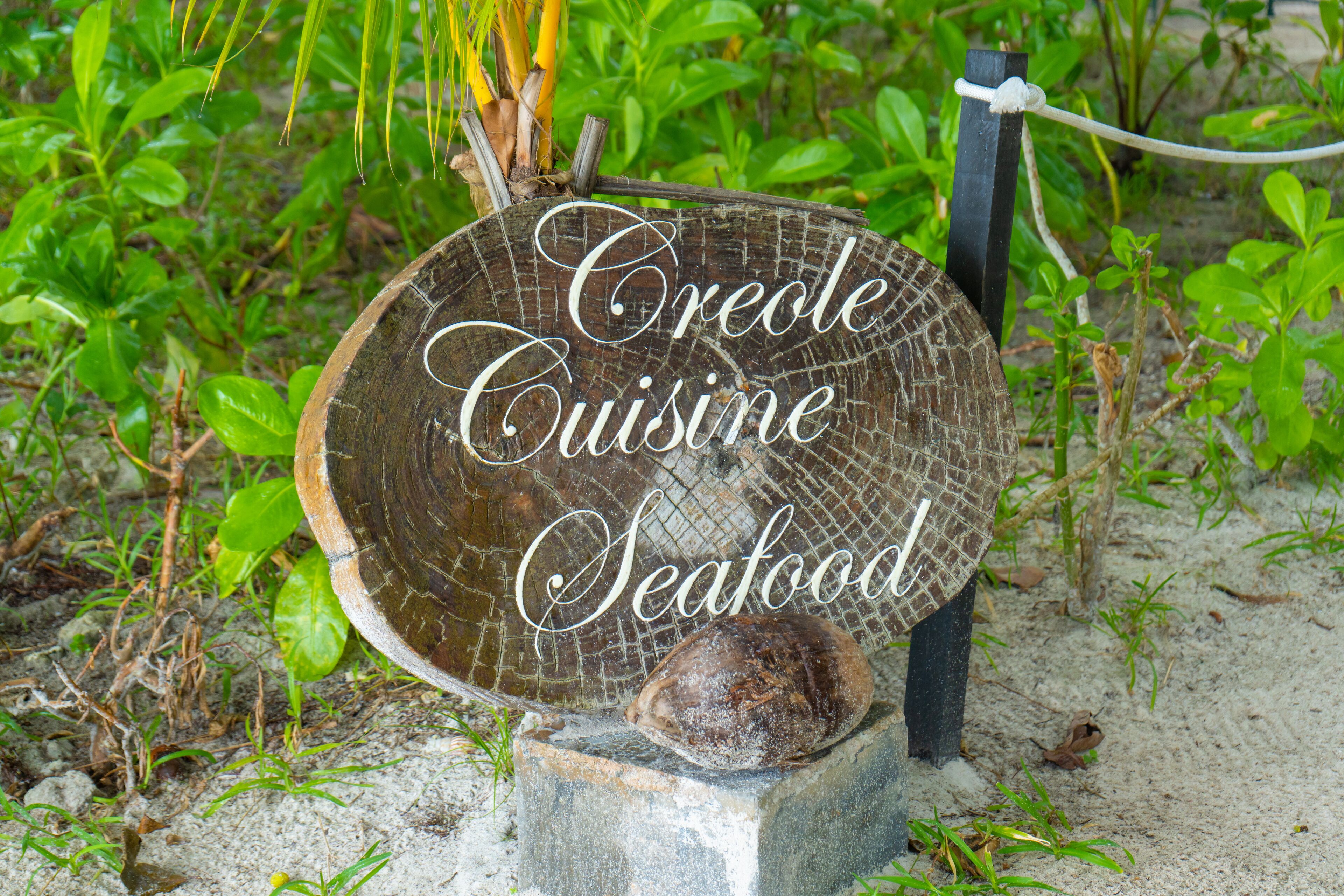 Uma placa de madeira com o texto 'Creole Cuisine Seafood' fixada em uma base de concreto.